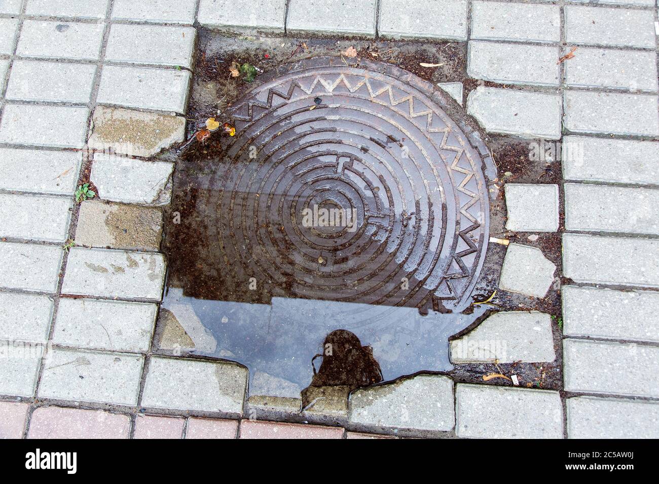 iron round manhole cover in a puddle of water on a pedestrian sidewalk ...