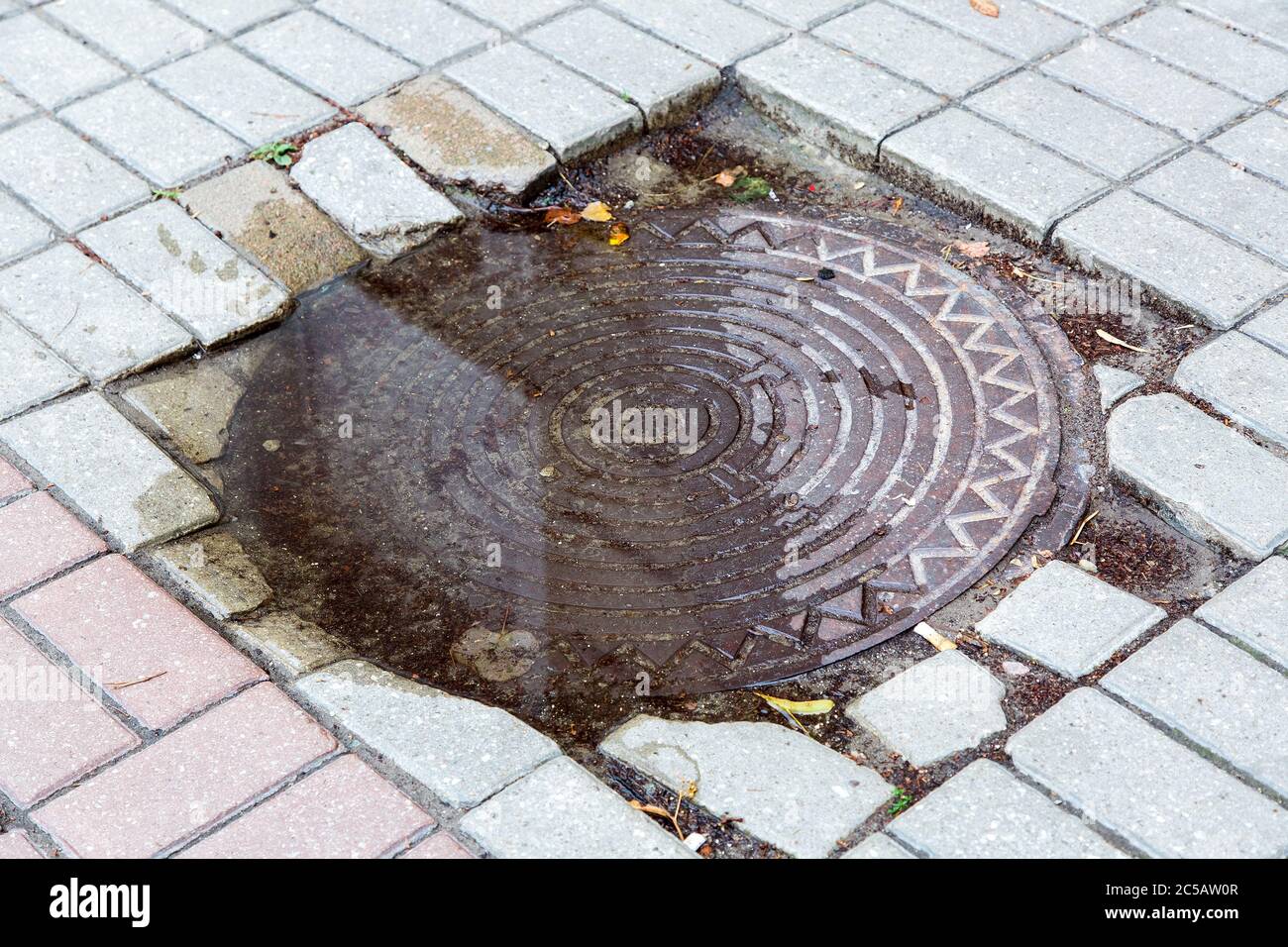 iron round manhole cover in a puddle of water on a pedestrian sidewalk ...