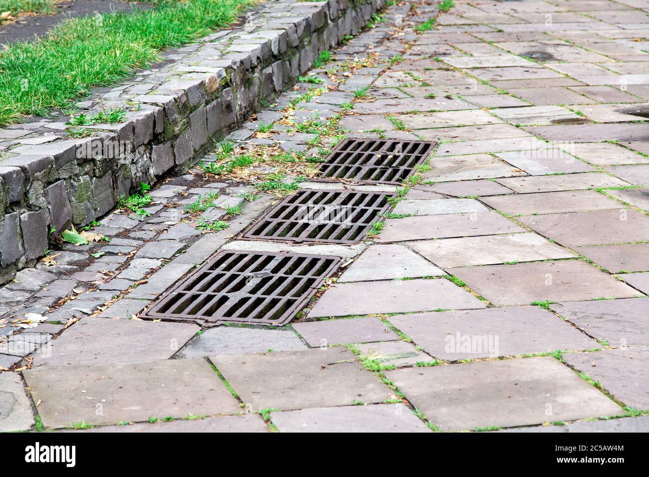 the iron grate of the drainage system hatch on the footpath paved with ...