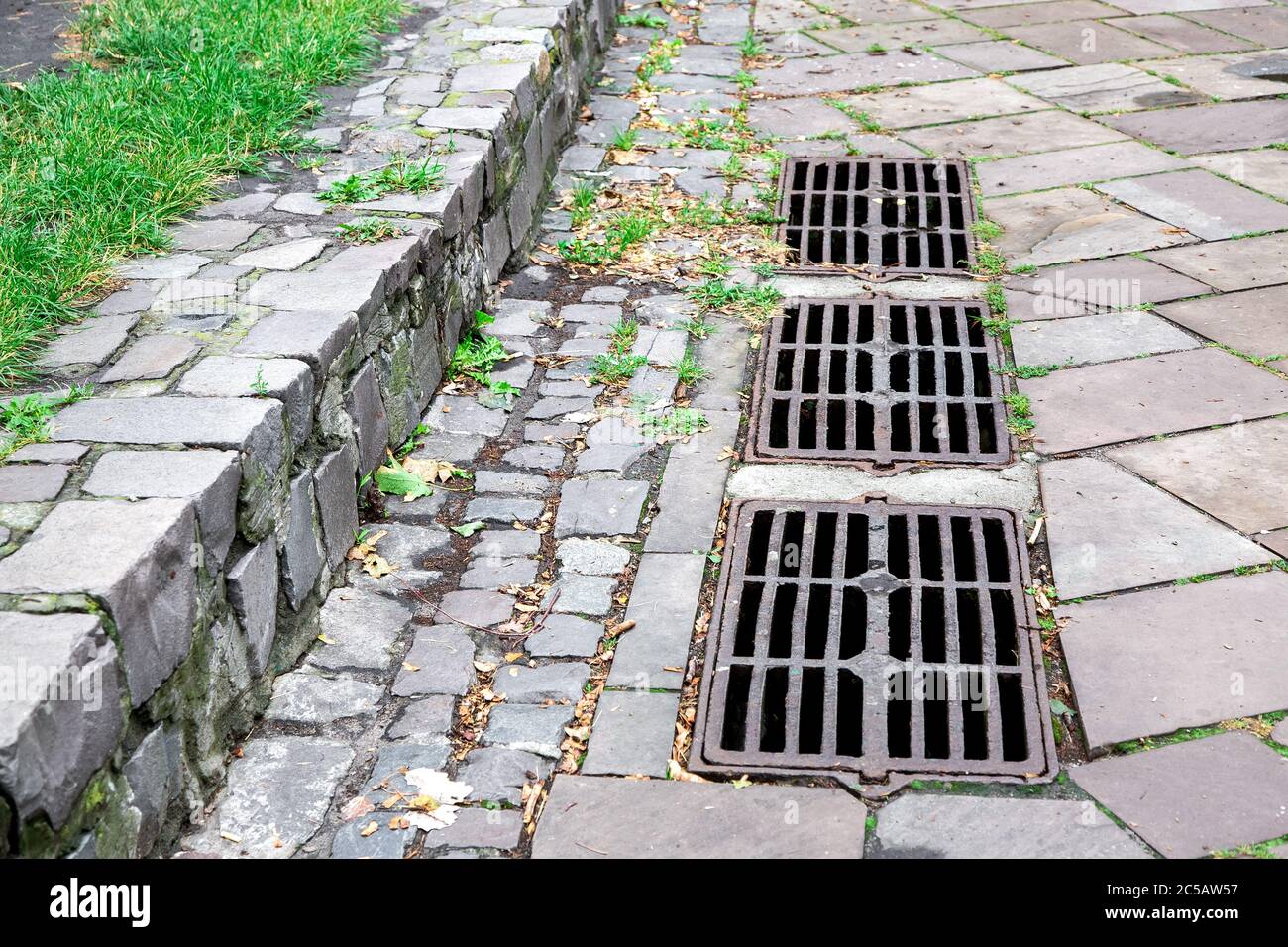 the iron grate of the drainage system hatch on the footpath paved with ...
