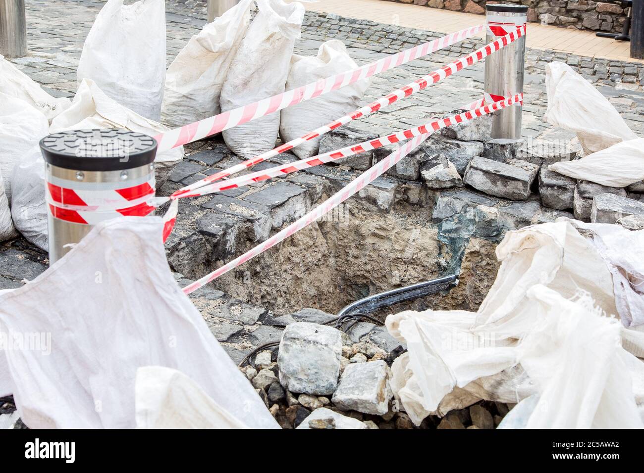 repair pit on the road of stone pavers with bollard fenced with striped ...