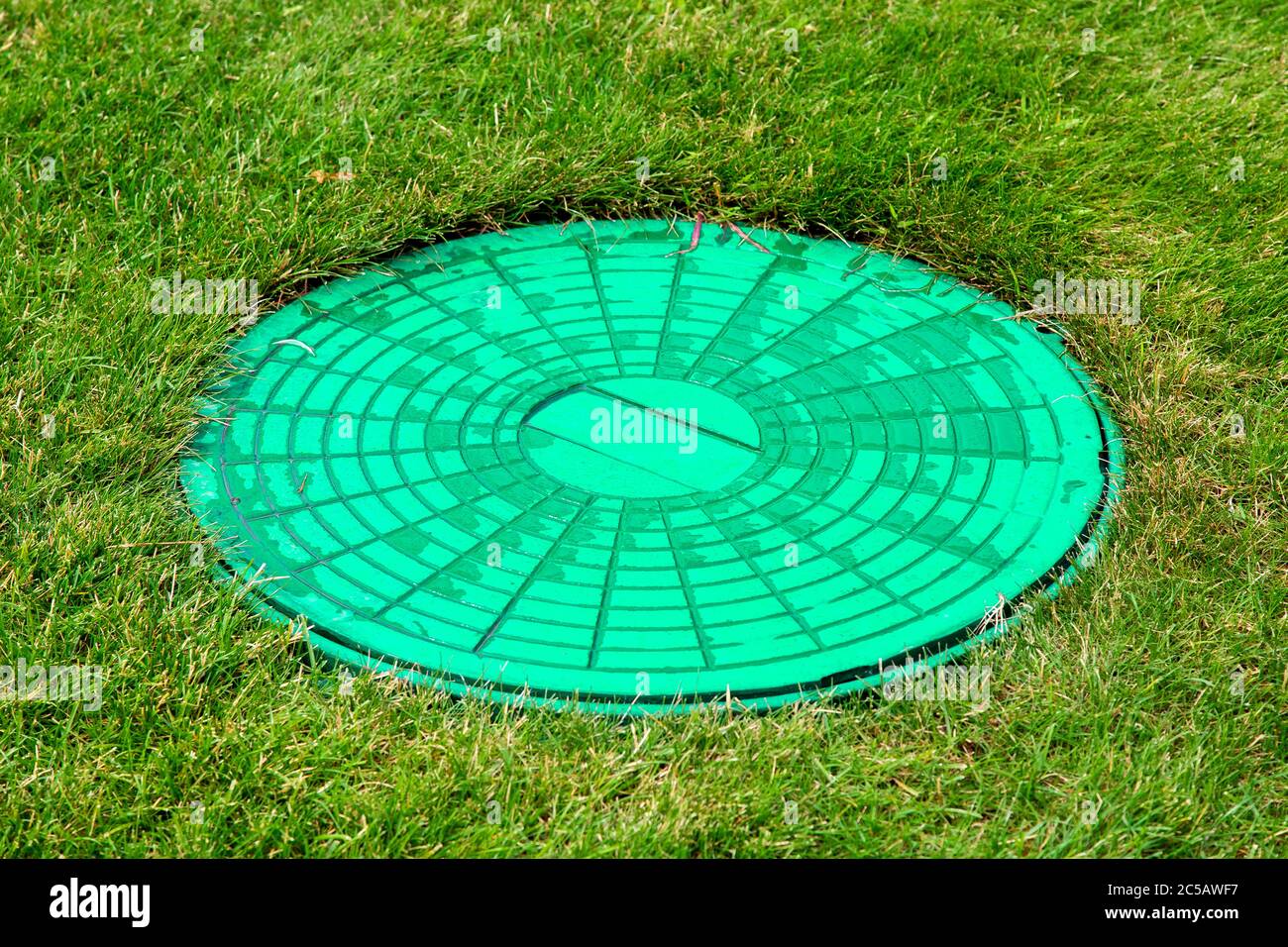 Green hatch of a sewer system in a clearing with green grass, close up ...