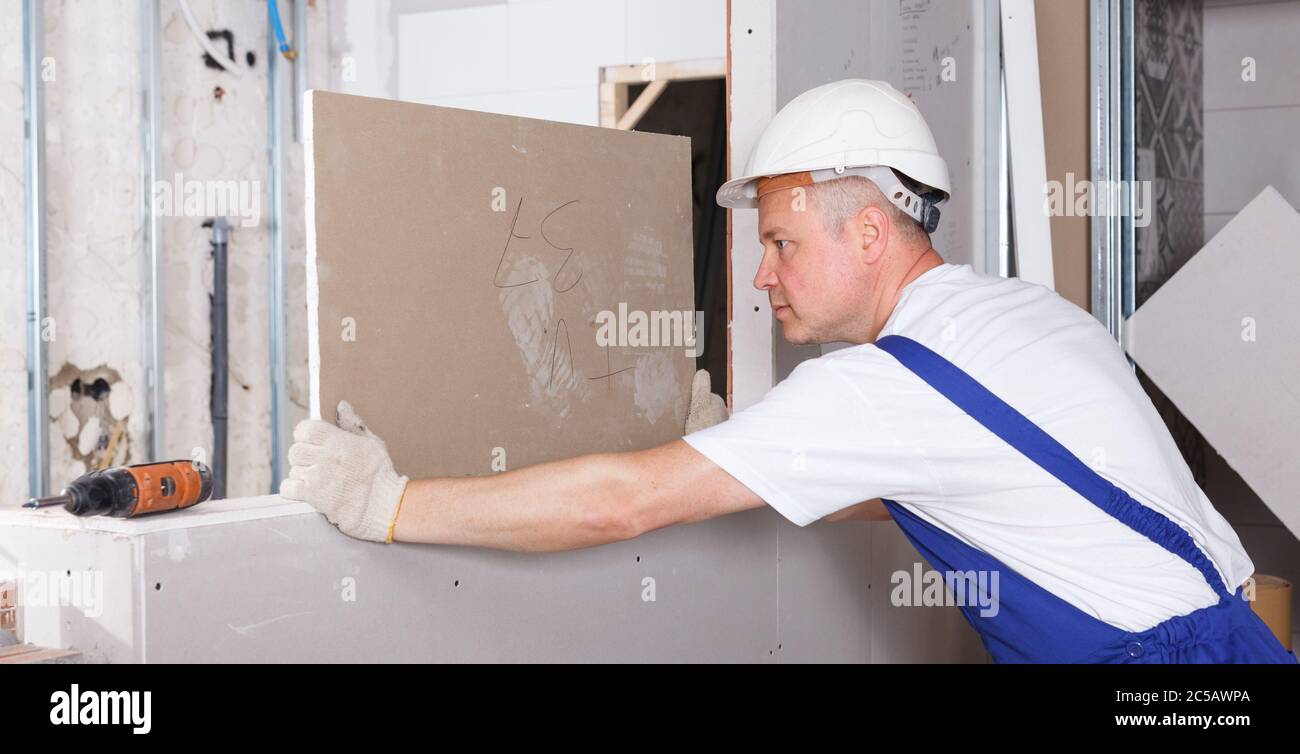 Construction worker engaged in drywall mounting in overhauls indoors ...