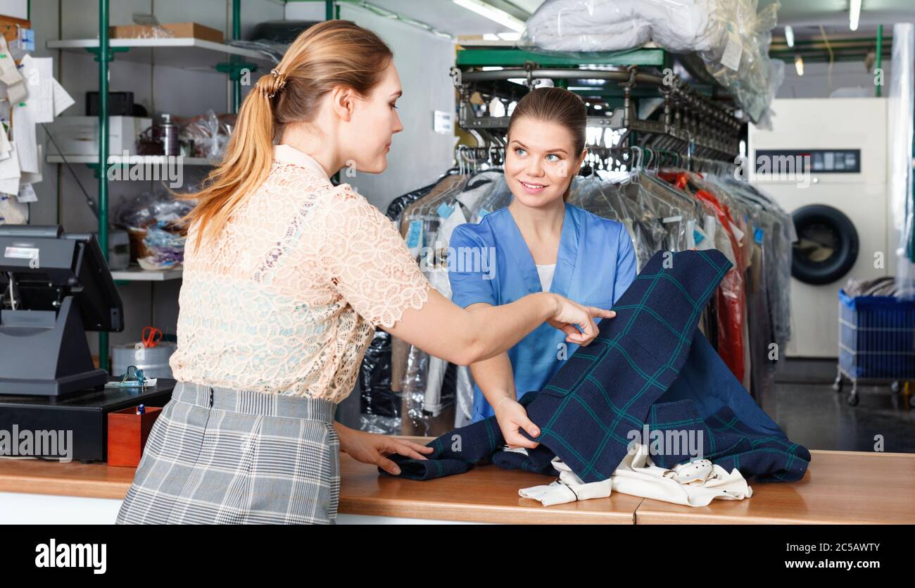 Young diligent woman worker of laundry taking clothes for dry cleaning ...