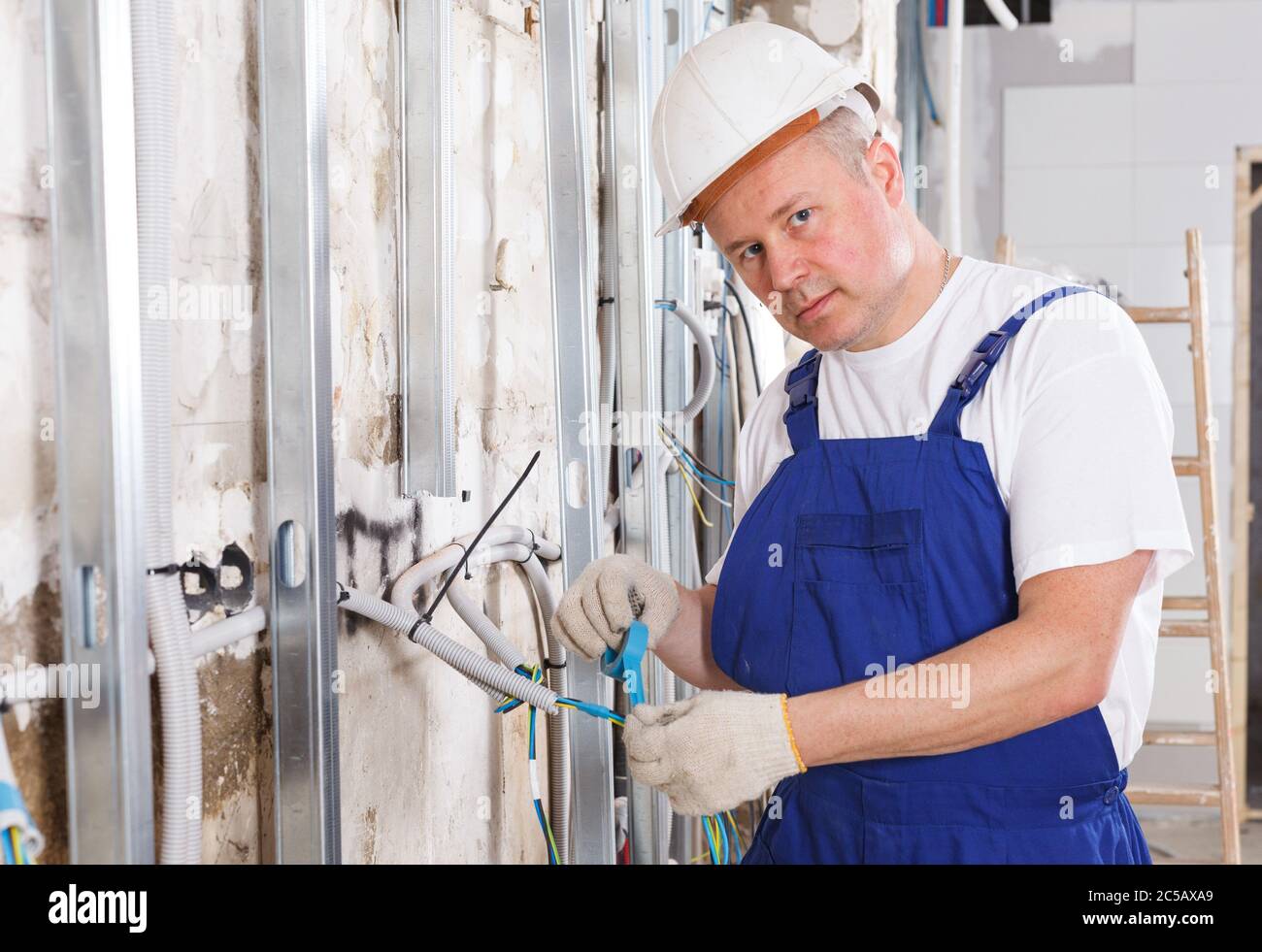 Confident electrician mounting electrical wiring inside building in ...