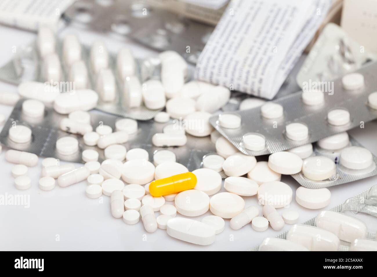 Yellow drug capsule lying among white tablets. Conceptual image of ...