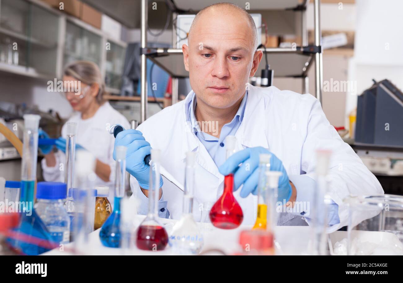 Focused lab technician working with reagents in test tubes during ...