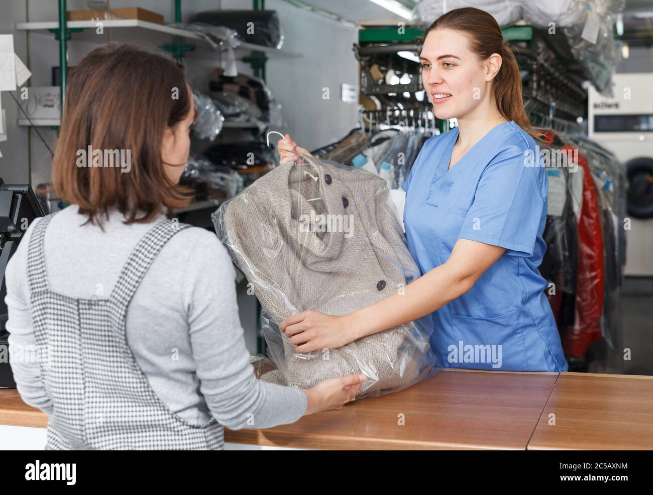 Female worker of dry cleaner returning clean clothes to customer on ...