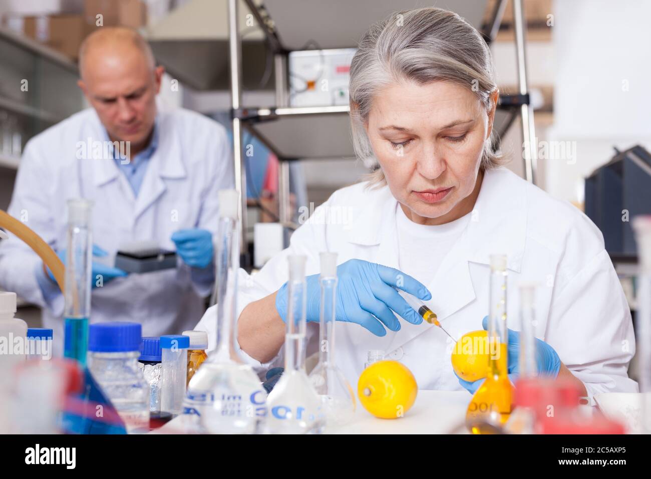Focused female lab technician injecting reagent from syringe into lemon ...