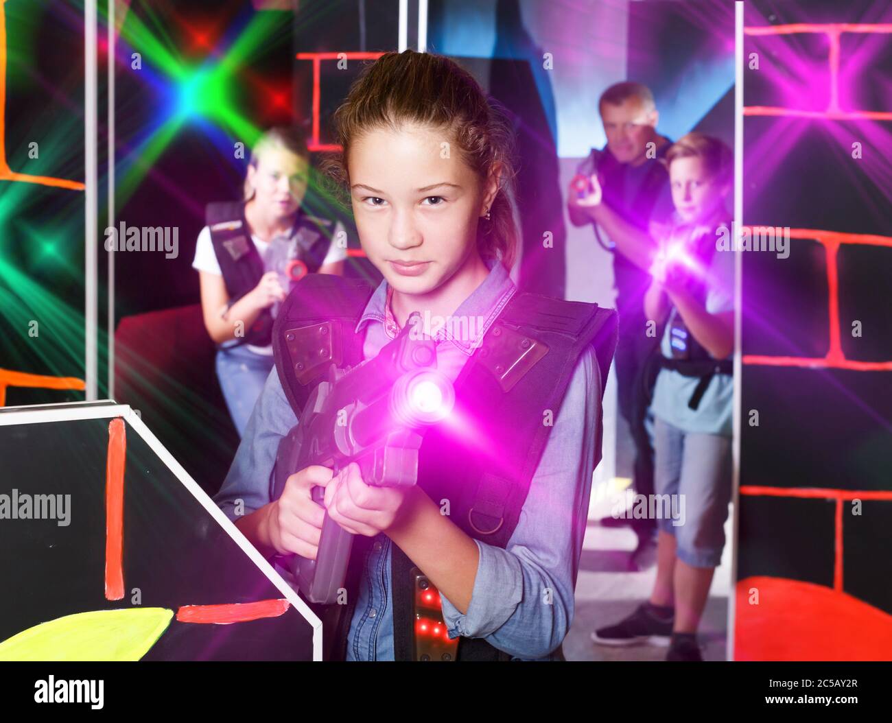 Excited girl aiming laser gun at other players during laser tag game in ...