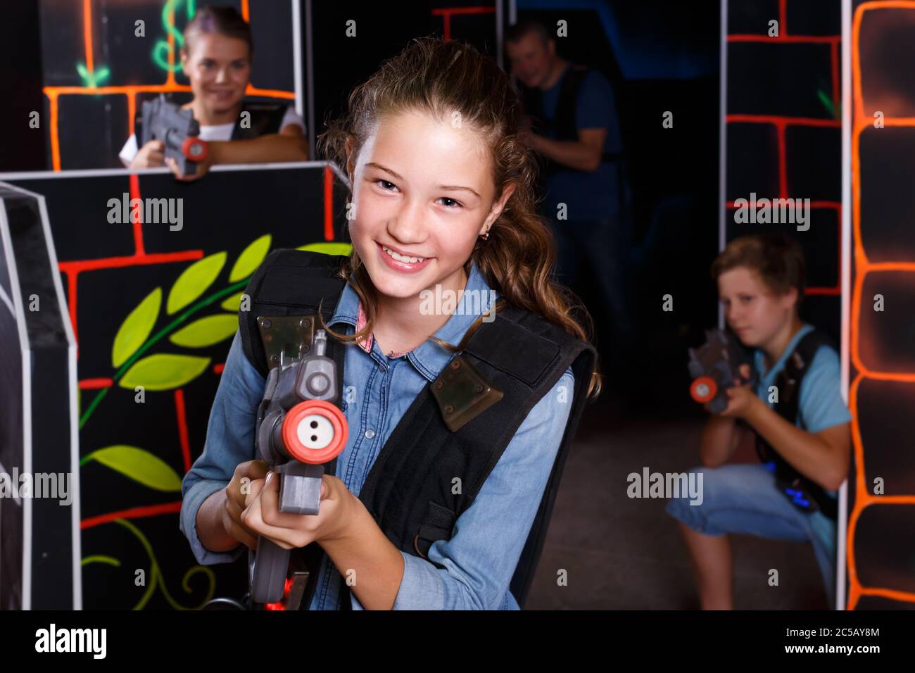 Glad girl aiming laser gun at other players during laser tag game in ...