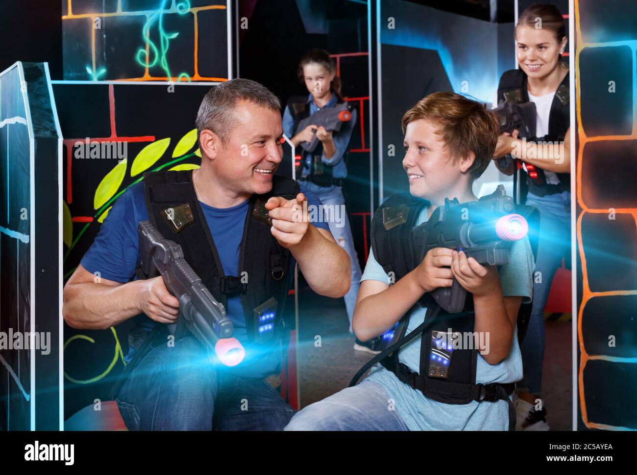 Modern young father and teen son with laser pistols playing laser tag ...