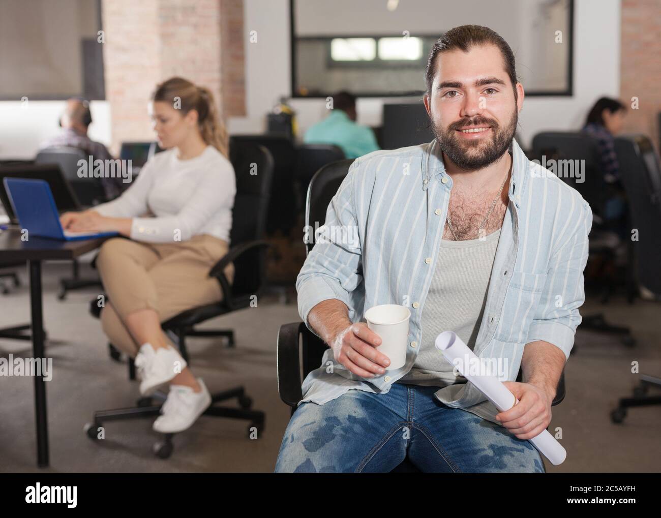 Portrait of smiling Latin hipster guy in coworking space with working ...