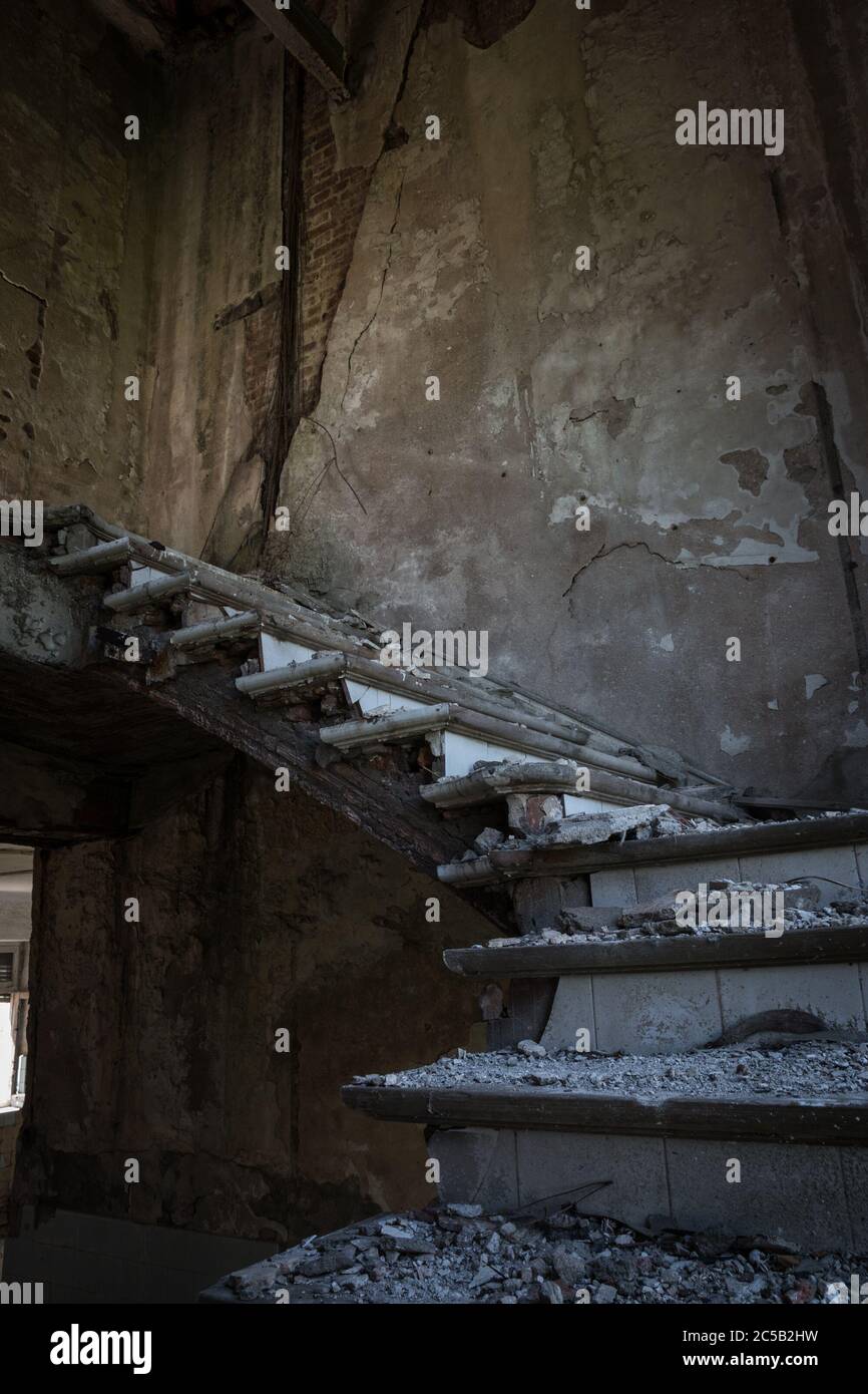 Vertical shot of a staircase with debris and cracked walls inside of an ...
