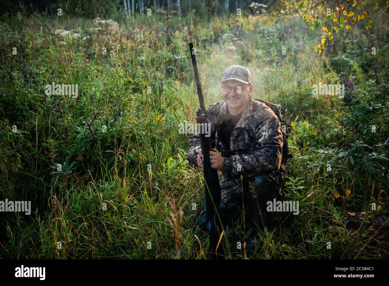 The smiling hunter or military person with gun or rifle in summer ...