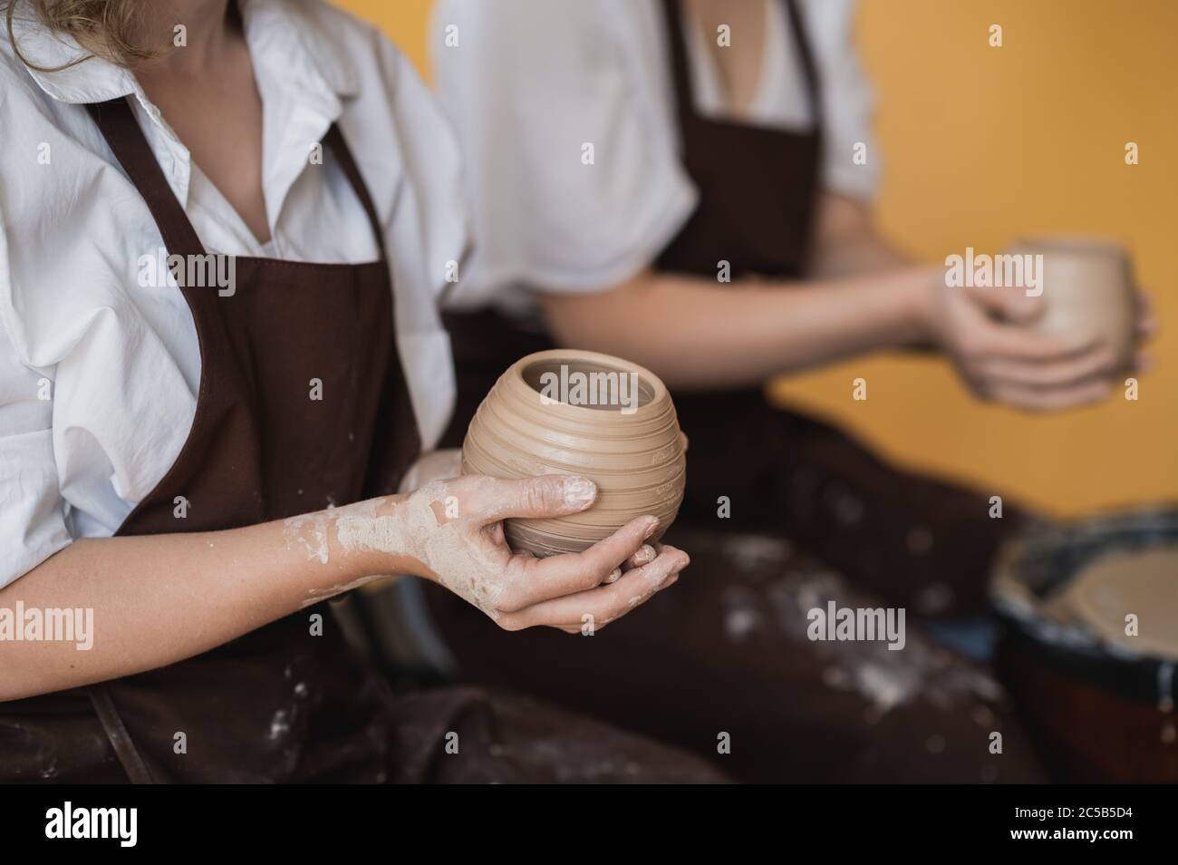 Two women make pottery on a pottery wheels, shaping clay by their hands ...