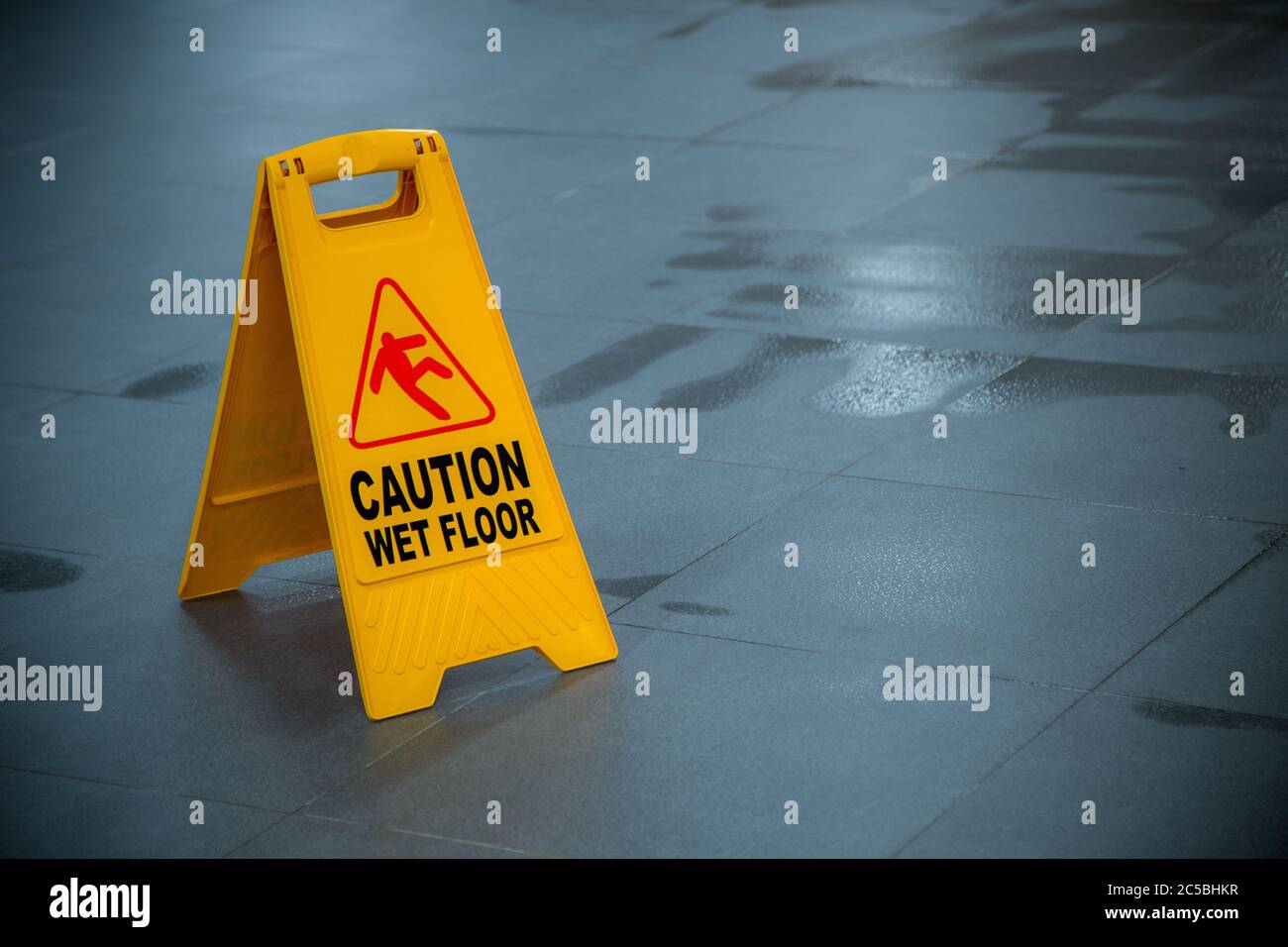 Yellow wet floor caution and no entry sign during rain with puddle of ...
