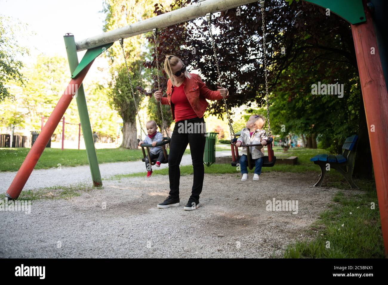 Happy Vivacious Young Mother With Her Baby Girl and Boy Twins Playing Together Outdoors in a ...