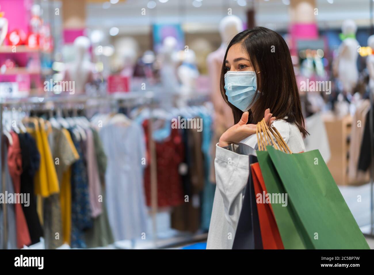 young woman holding shopping bag and looking to clothes at mall and her ...