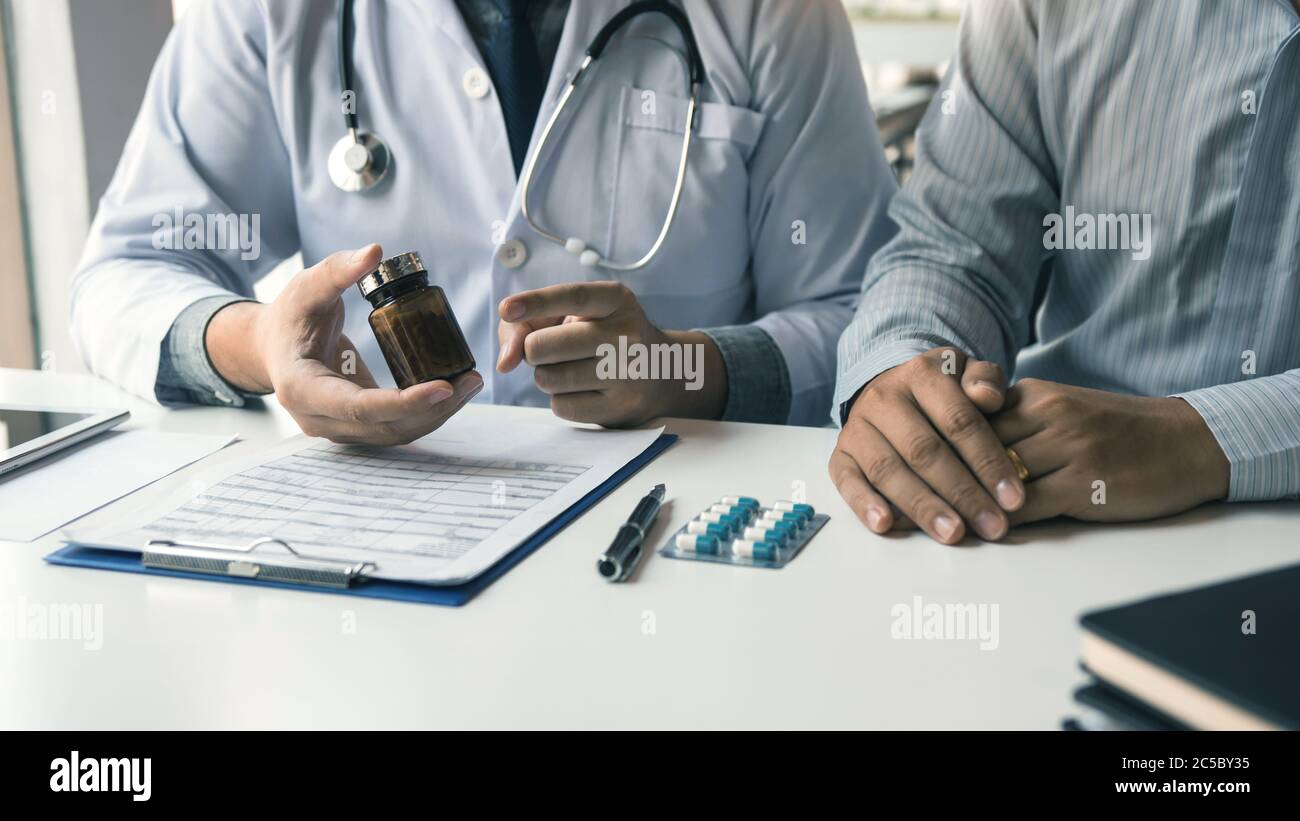 Confident doctor man holding a pill bottle and writing while talking ...