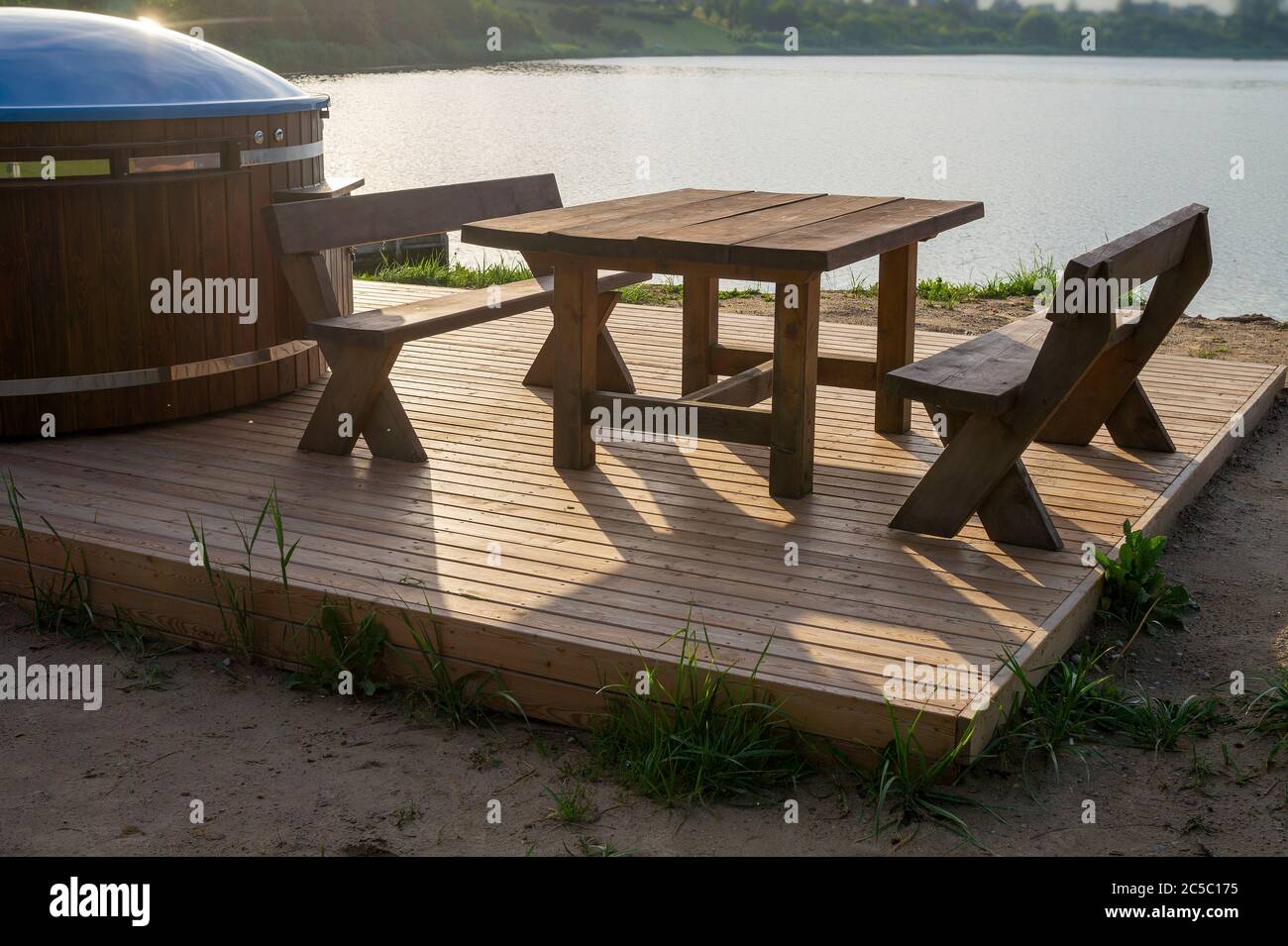 Vacant wooden table and chairs on a deck overlooking a lake or river in ...