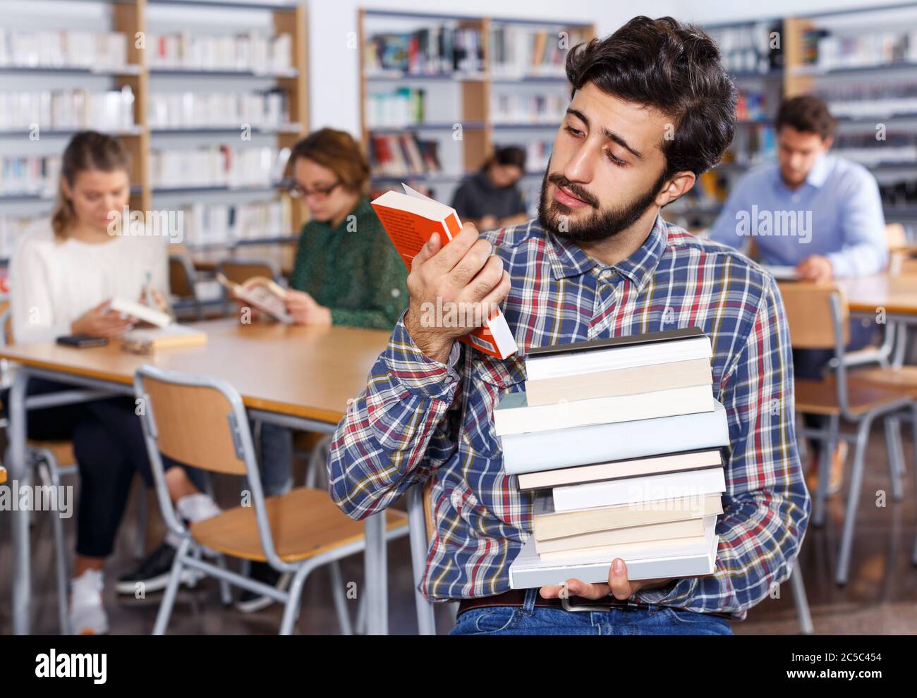 weary upset man with stack of books in hands in public library Stock ...