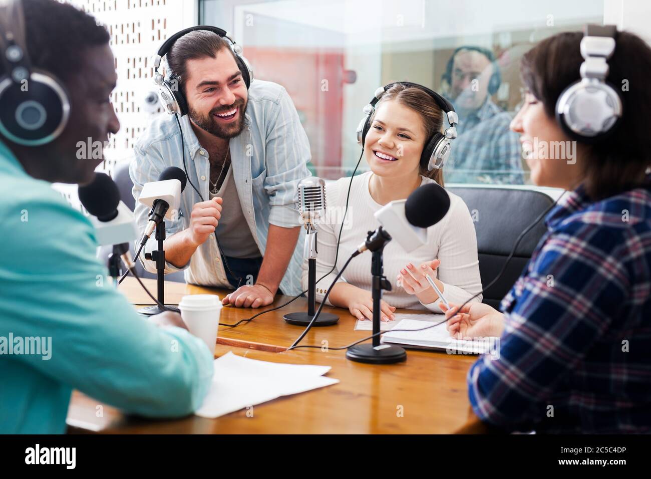 Smiling international team of radio presenters interviewing guest in ...