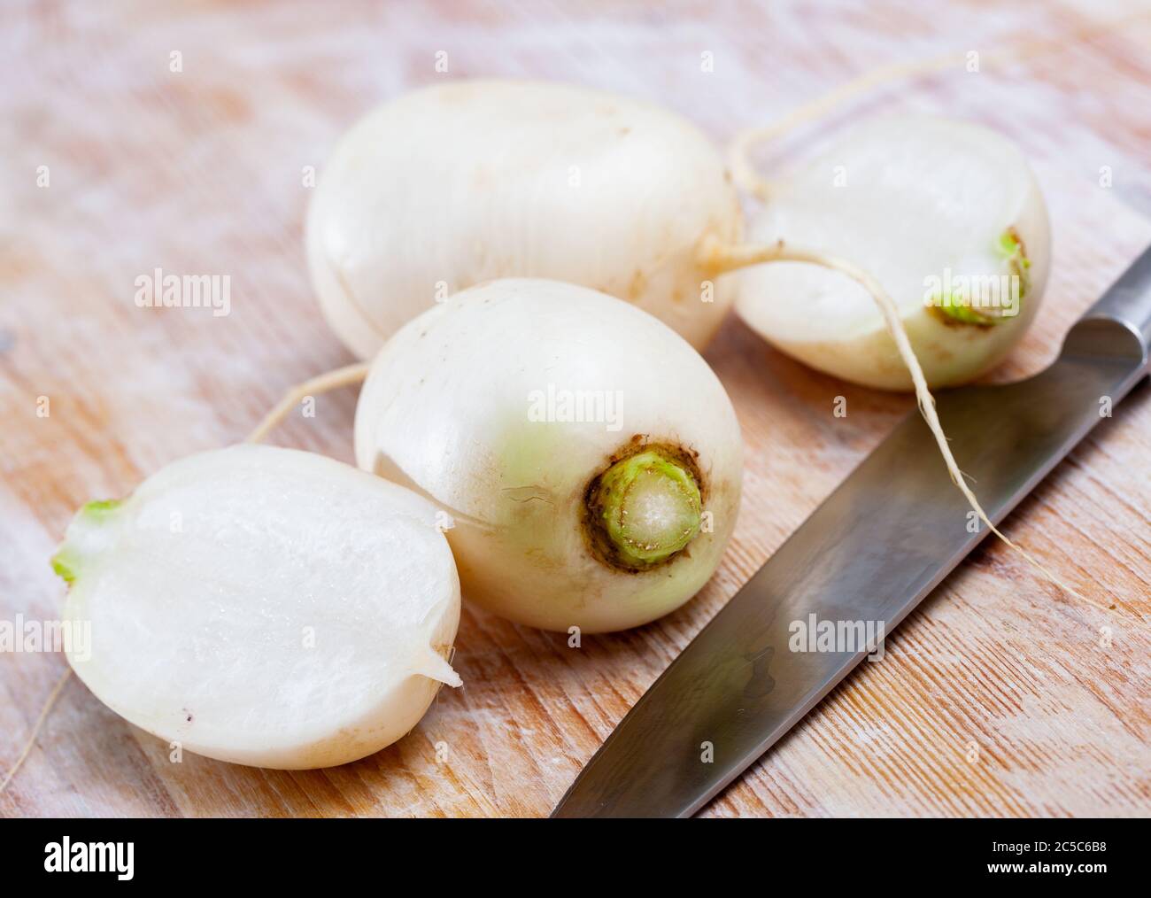 Closeup of whole and halved organic white radishes on wooden surface ...