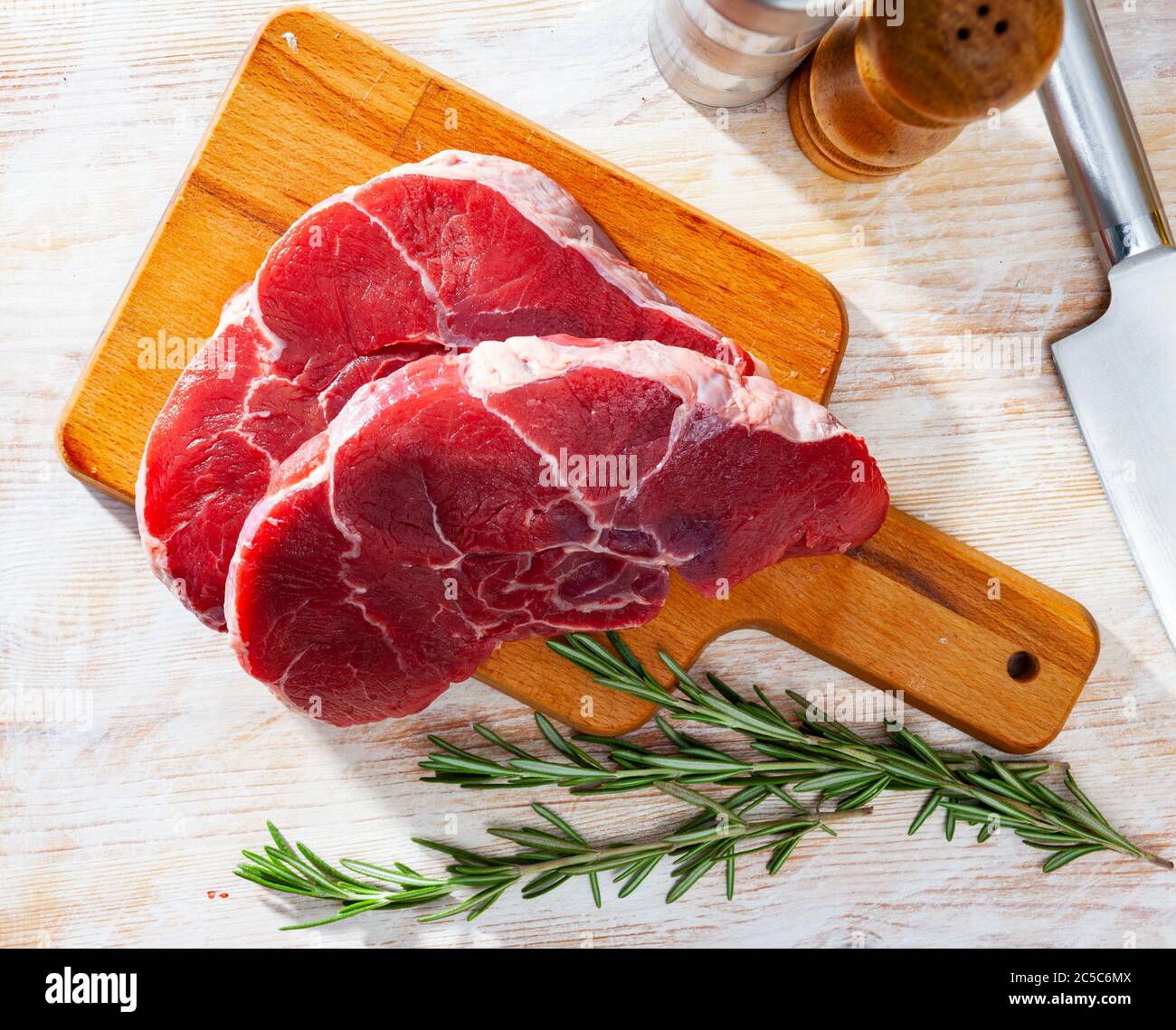 Raw juicy veal steaks with herbs ready for cooking on wooden table ...
