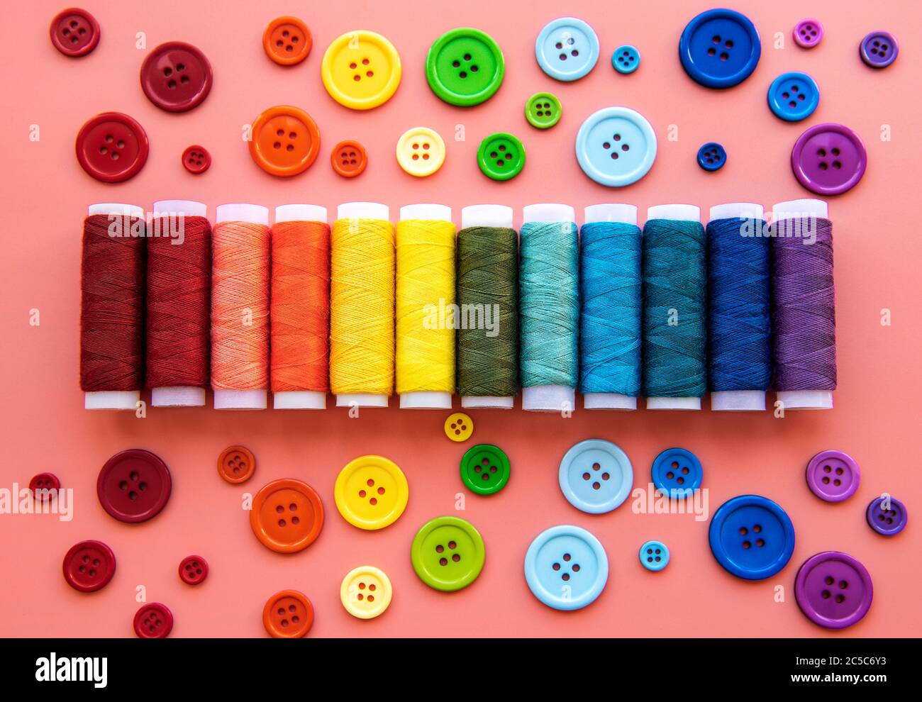 Spools of thread and buttons on the colors of the rainbow on a pink ...
