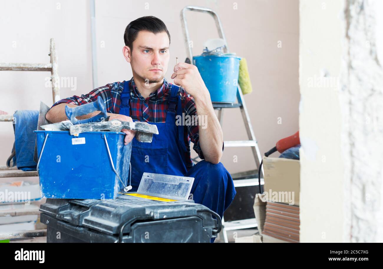 Serious worker repairing room and looking for necessary tool in toolbox ...
