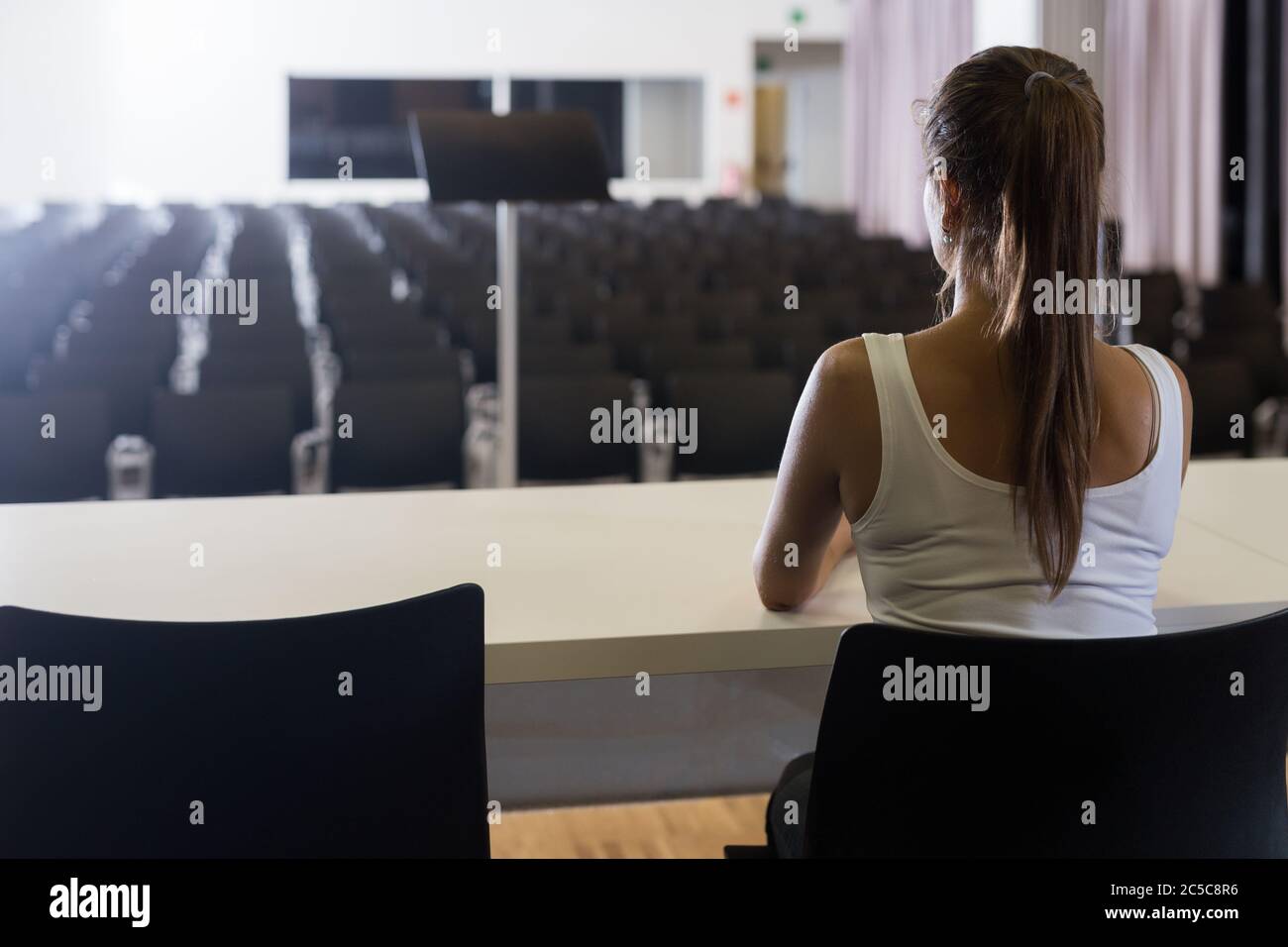 Young woman sitting at the table on stage opposite to empty conference ...