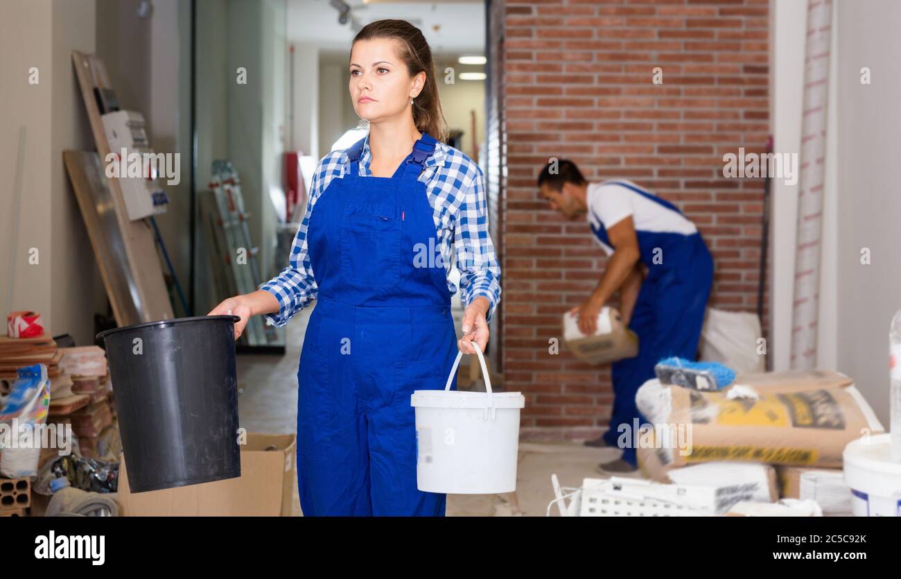 Young positive female worker holding buckets during doing finishing ...