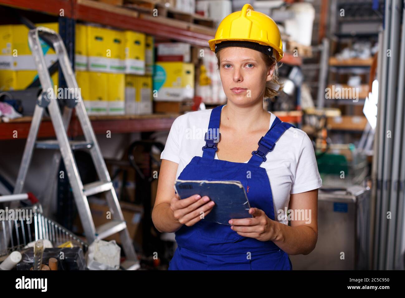 Portrait of female worker in uniform and helmet standing near shelves ...