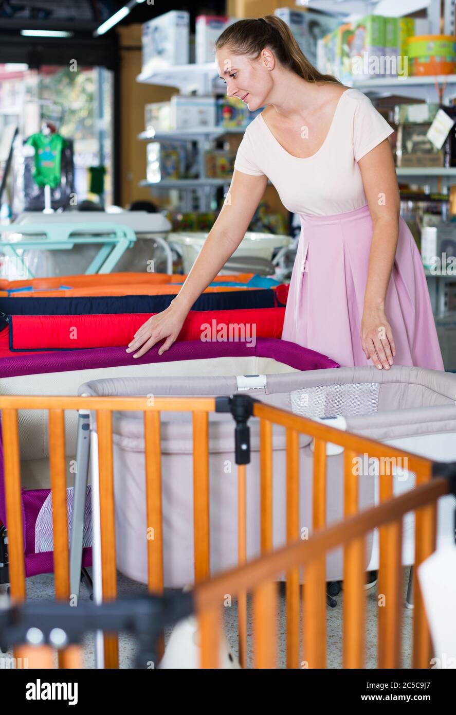 Smiling young pregnant woman selecting playpen for future baby in ...