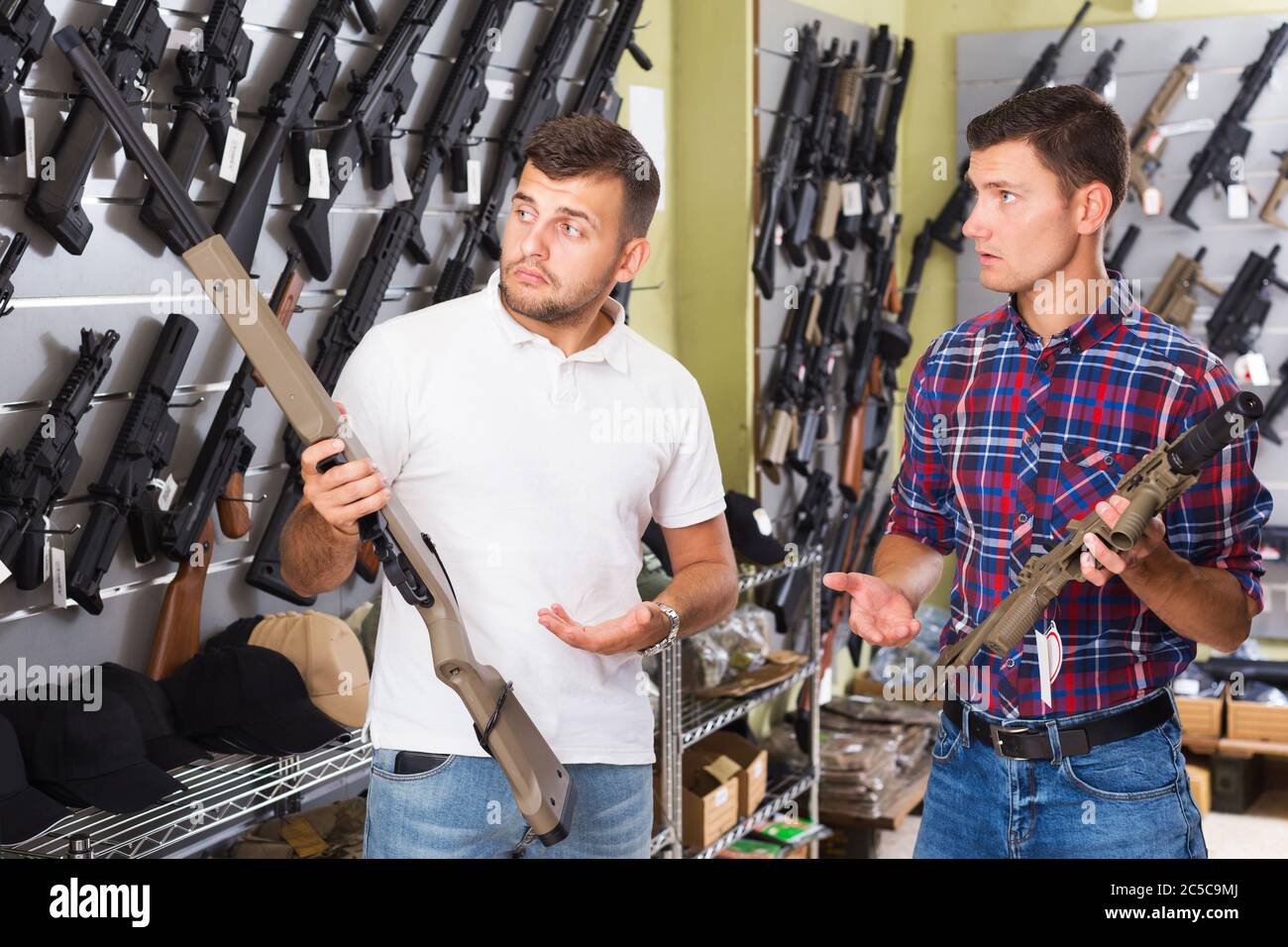 Portrait of two serious male friends choosing air-powered gun in army ...