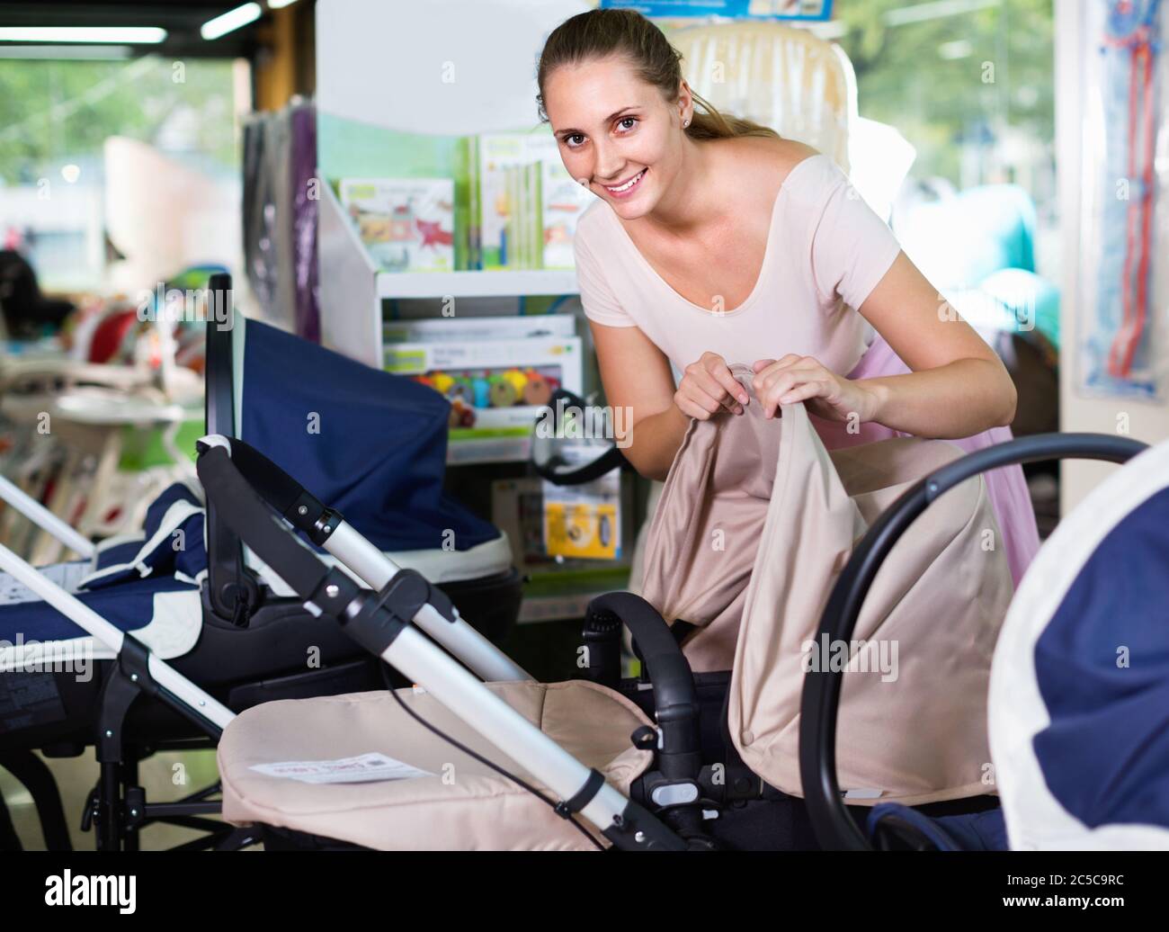 Happy cheerful smiling pregnant woman buying baby stroller in kids mall ...