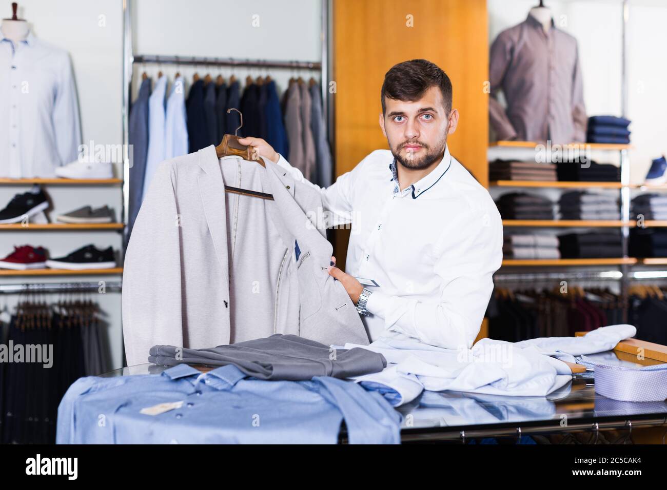 Smiling man seller showing various jacket in men clothes shop Stock ...
