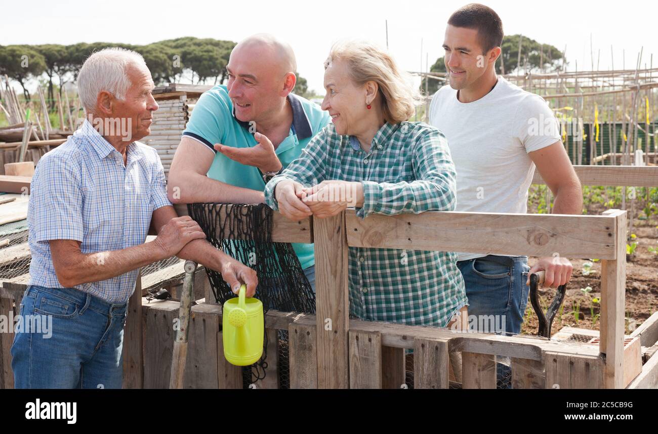 Family of four gardeners talking together near wooden fence in garden ...
