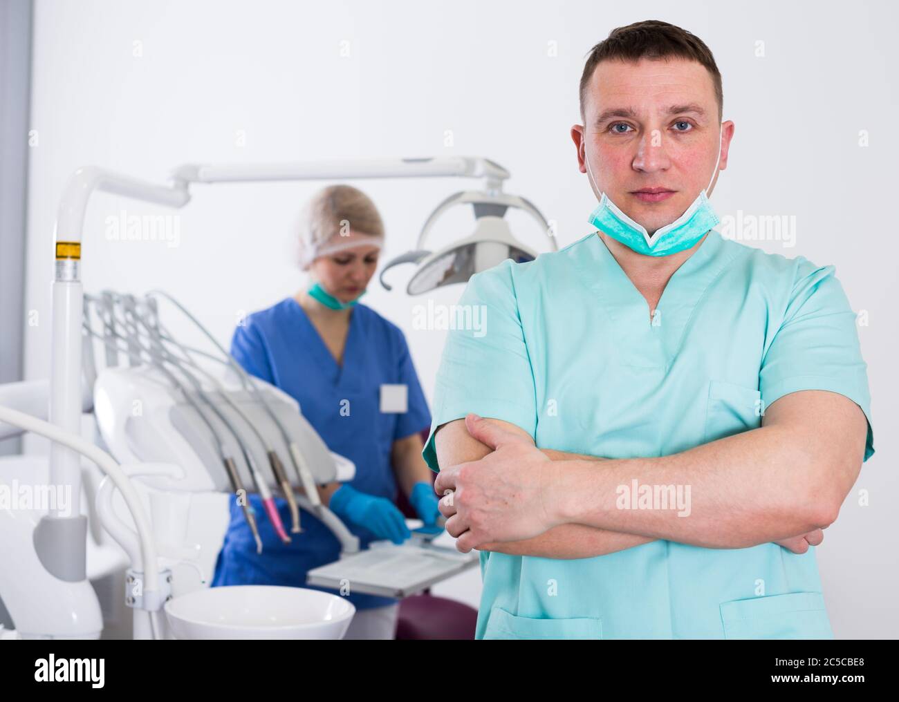 Portrait of professional male dentist with arms crossed in office with ...