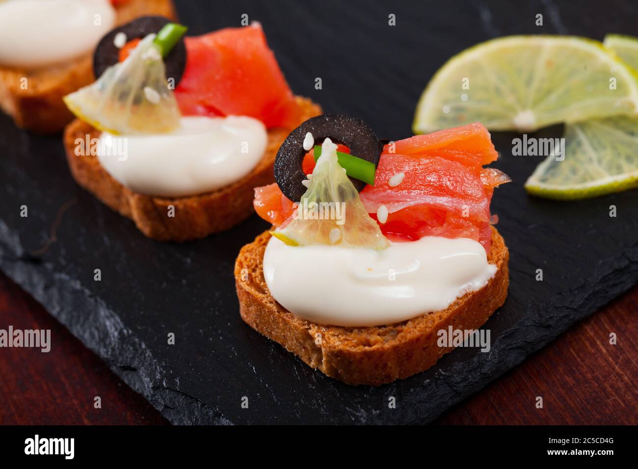 Canapes on toasted bread with smoked salmon, olives and creamy sauce on ...