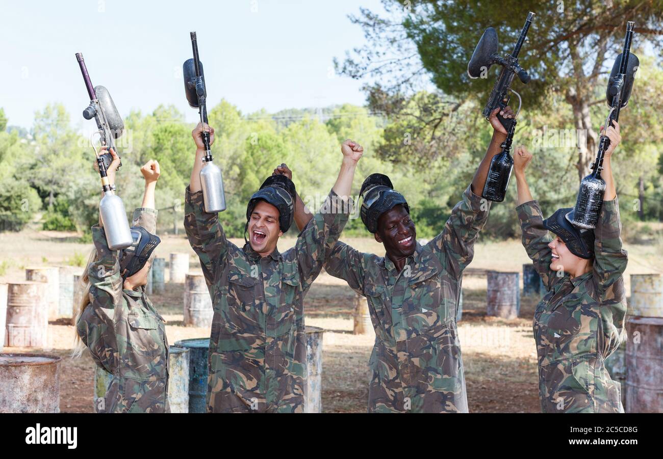 Portrait of happy paintball players wearing uniform and holding guns ...