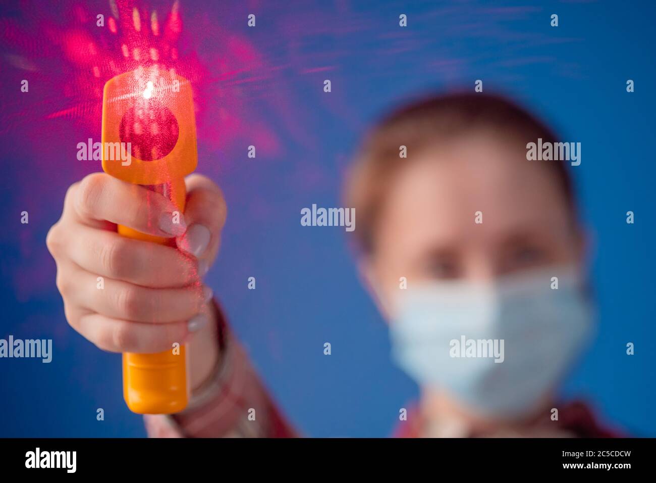Woman in medical face mask holding yellow pyrometer to measure ...