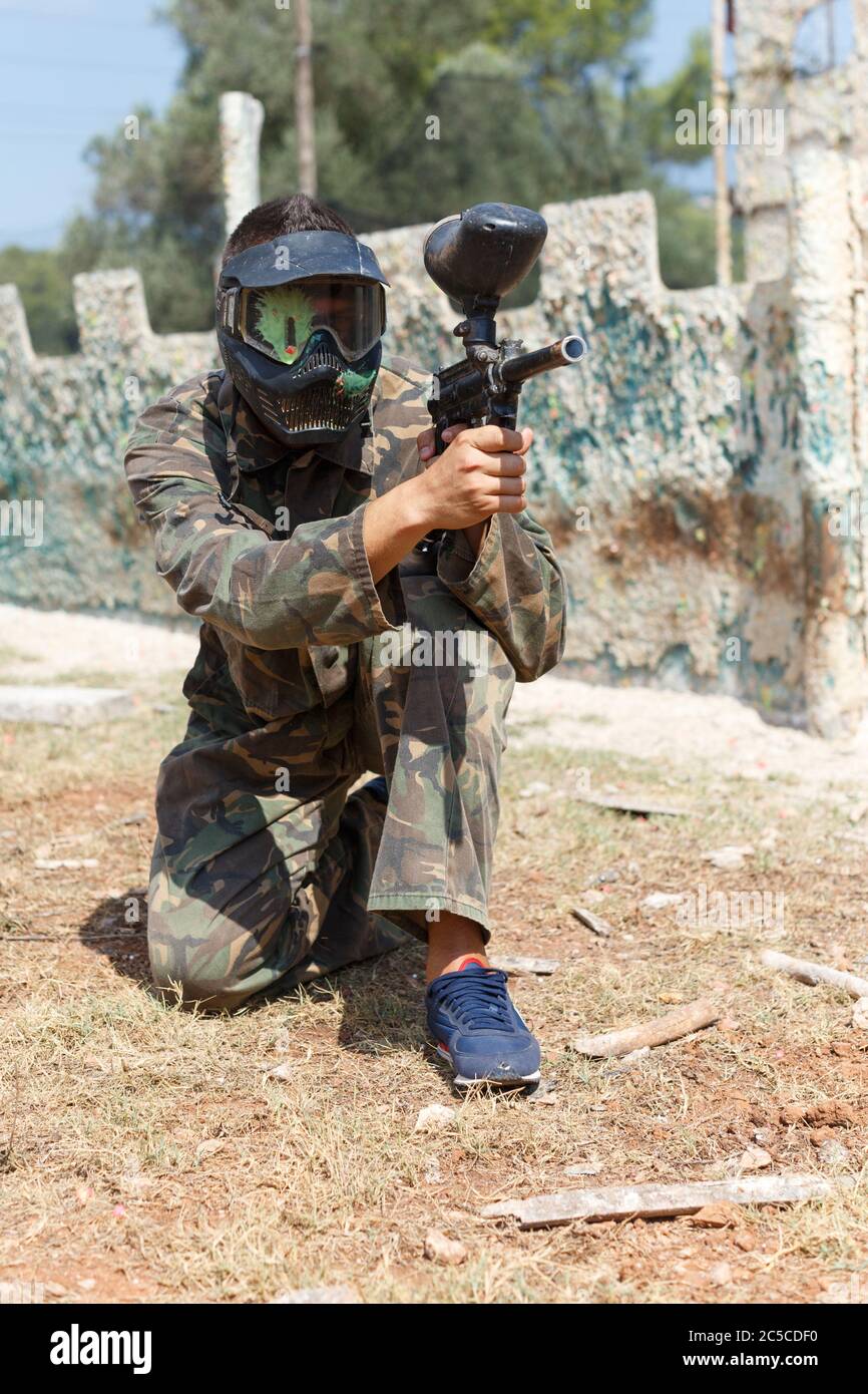 Male paintball player aiming and shooting with gun at opposing team ...