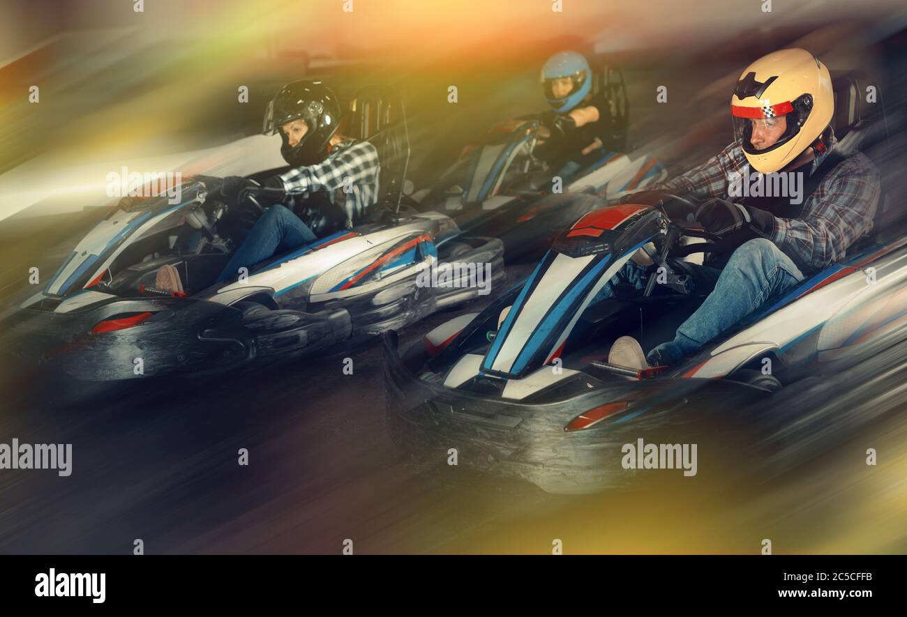 Young positive people in helmets driving racing cars for karting in ...