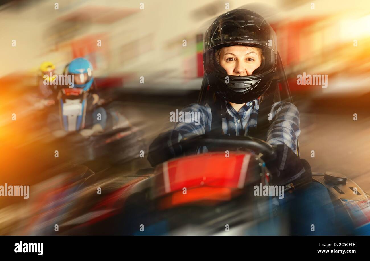 Cheerful positive smiling girl and her friends competing on racing cars ...