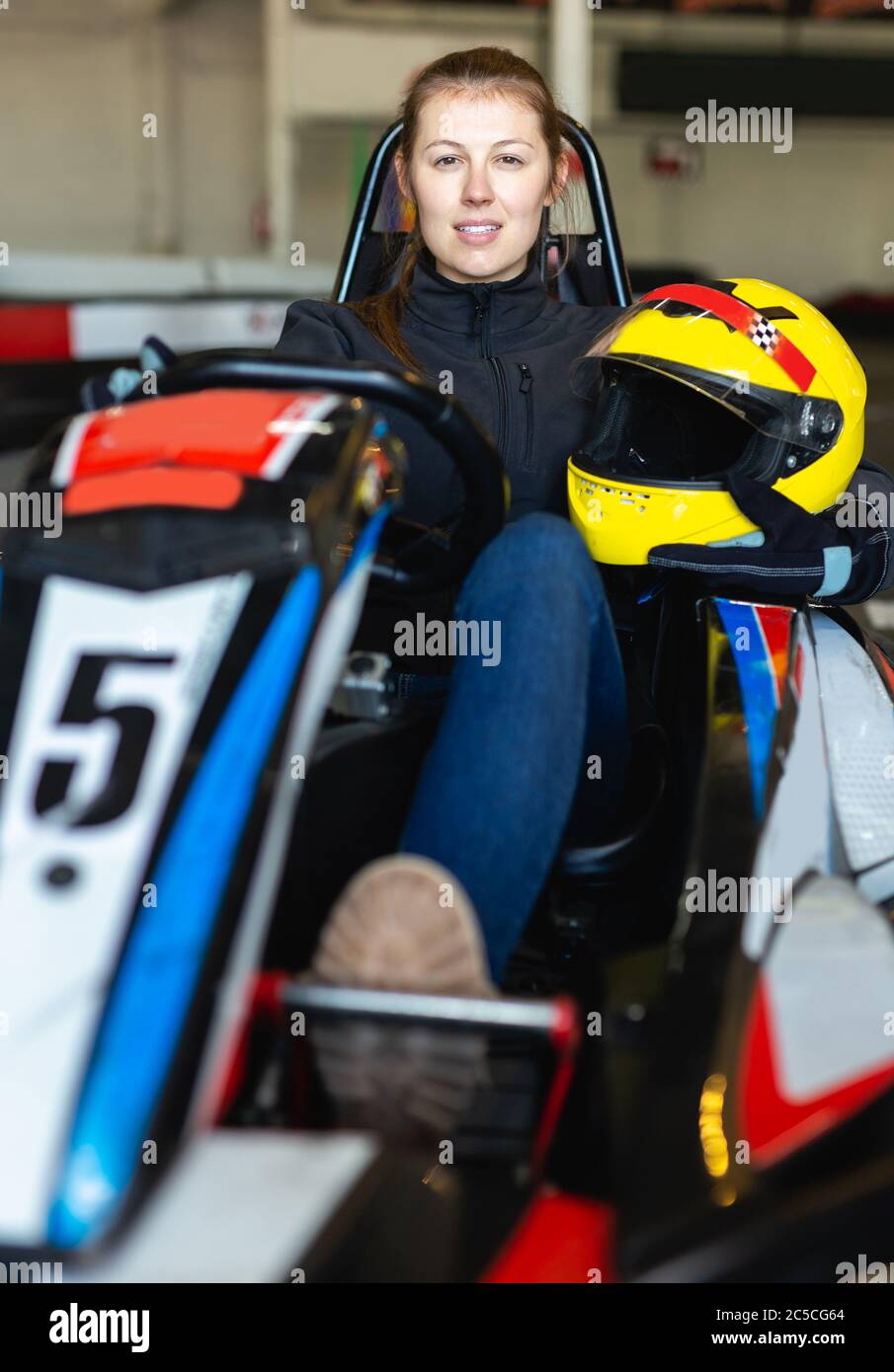 Cheerful adult girl posing with helmet in her hands at kart circuit ...