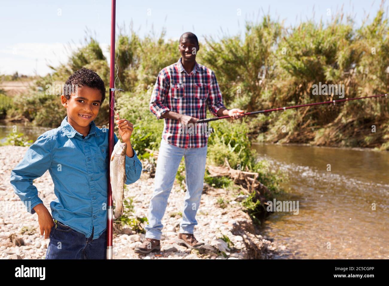 Portrait of afro fisherman and his little son holding fishing rod with ...