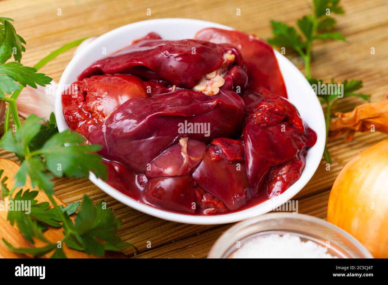 Picture of raw chicken liver with garlic and greens on wooden surface ...