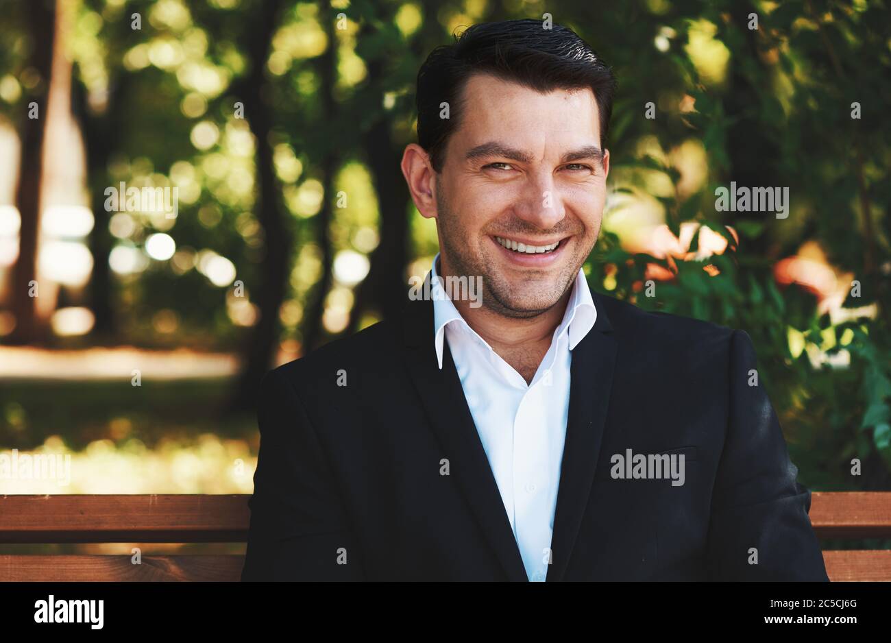 Handsome man in suit sitting on a bench in the park. Cheerful ...